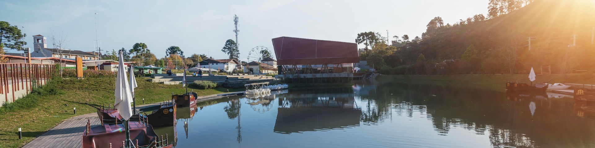 Um rio calmo com barcos atracados, uma roda gigante e um edifício moderno ao fundo.