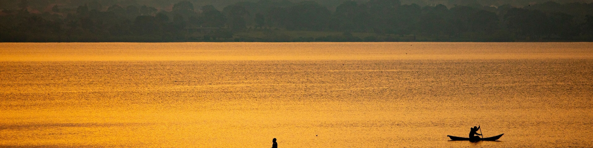 Água calma refletindo um pôr do sol dourado. Dois barcos são visíveis, um mais próximo do primeiro plano e outro ao longe.