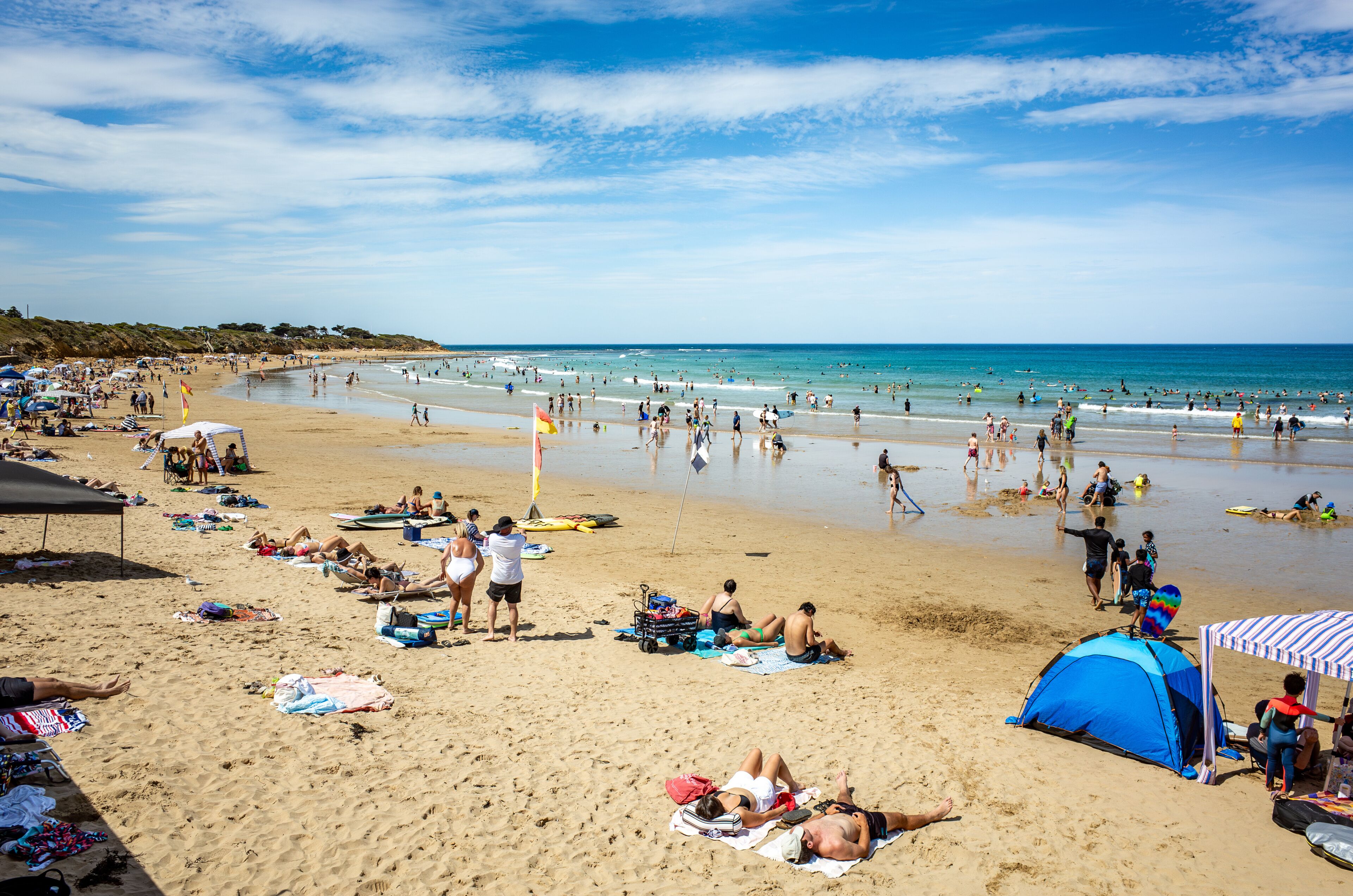 Uma praia cheia de gente se bronzeando, nadando e brincando.
