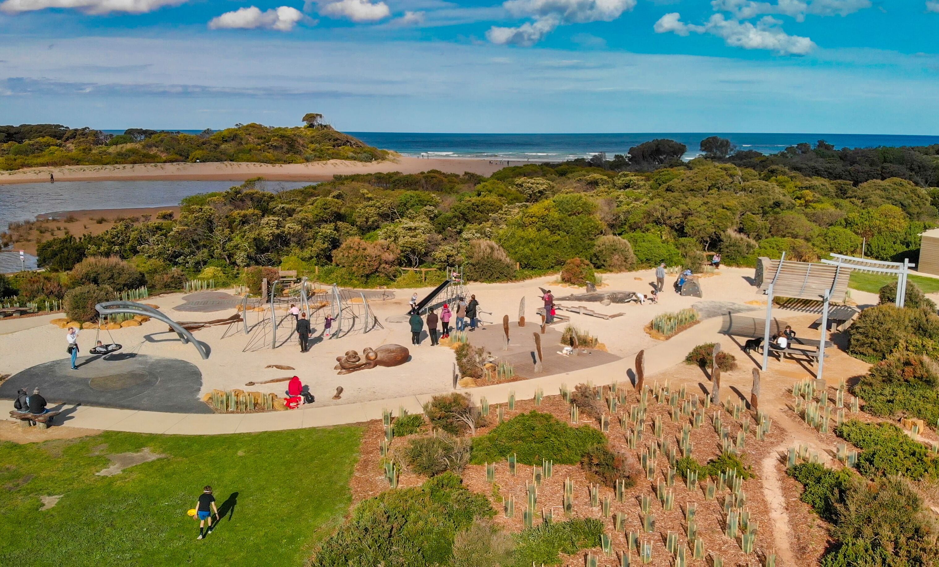 Um parque costeiro com uma praia de areia, parquinho e diversificada vegetação.