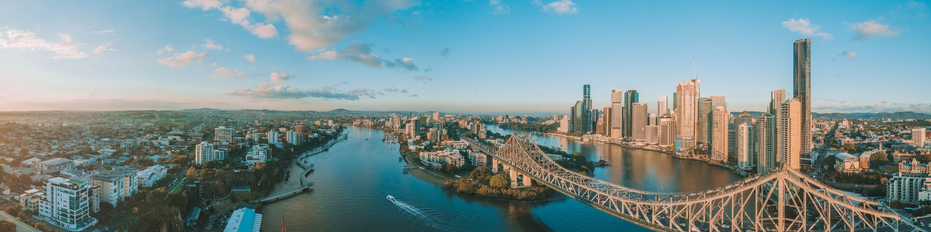 Paisagem urbana com uma ponte imponente sobre um rio, cercada por edifícios altos e um céu claro.