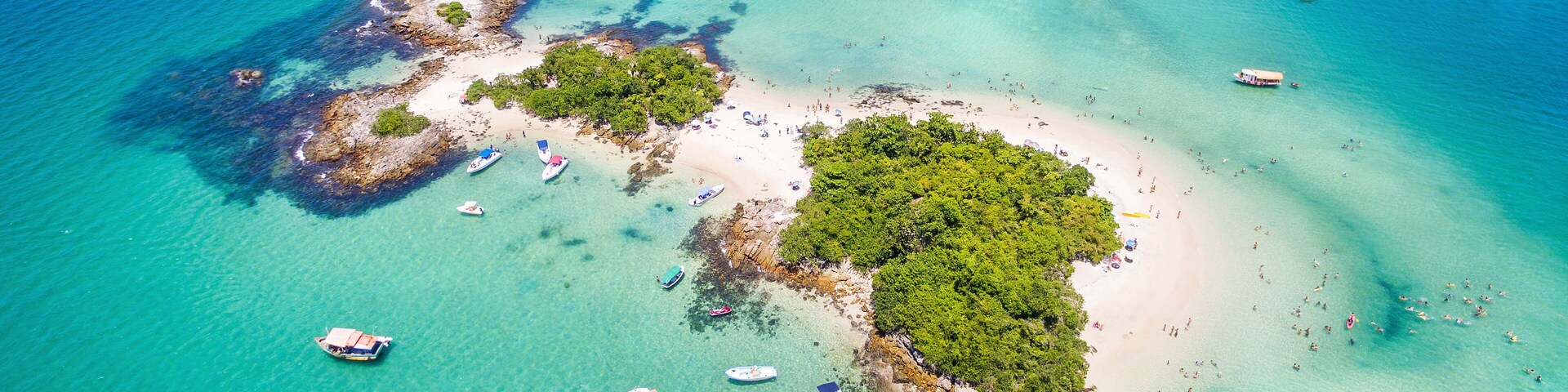 Vista aérea de uma ilha tropical com águas turquesa cristalinas, praias de areia e vegetação exuberante.
