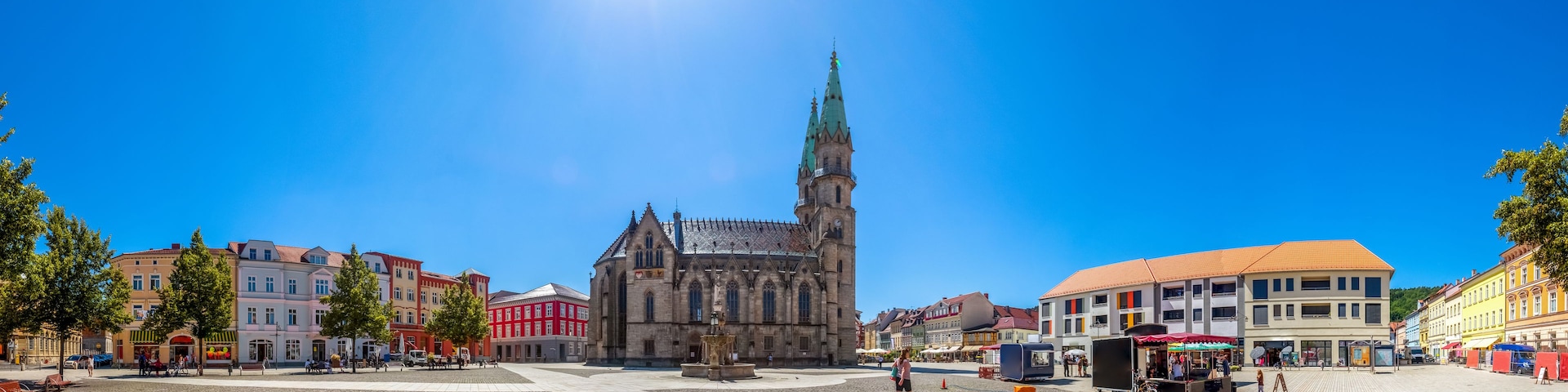 Uma igreja histórica com uma torre alta, praça de paralelepípedos e edifícios coloridos.
