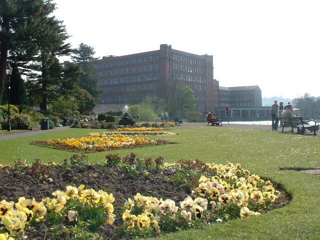 Um parque com canteiros de flores, bancos e um edifício ao fundo.