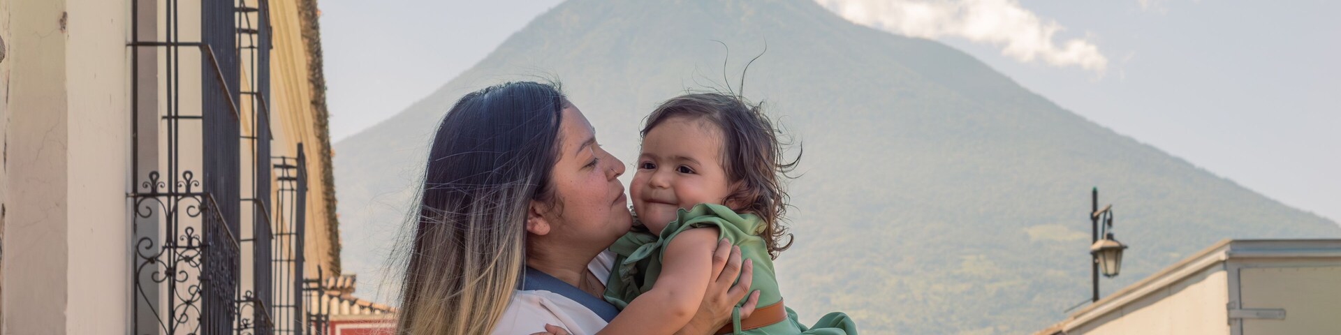 Uma mulher segurando uma criança em frente a uma montanha.