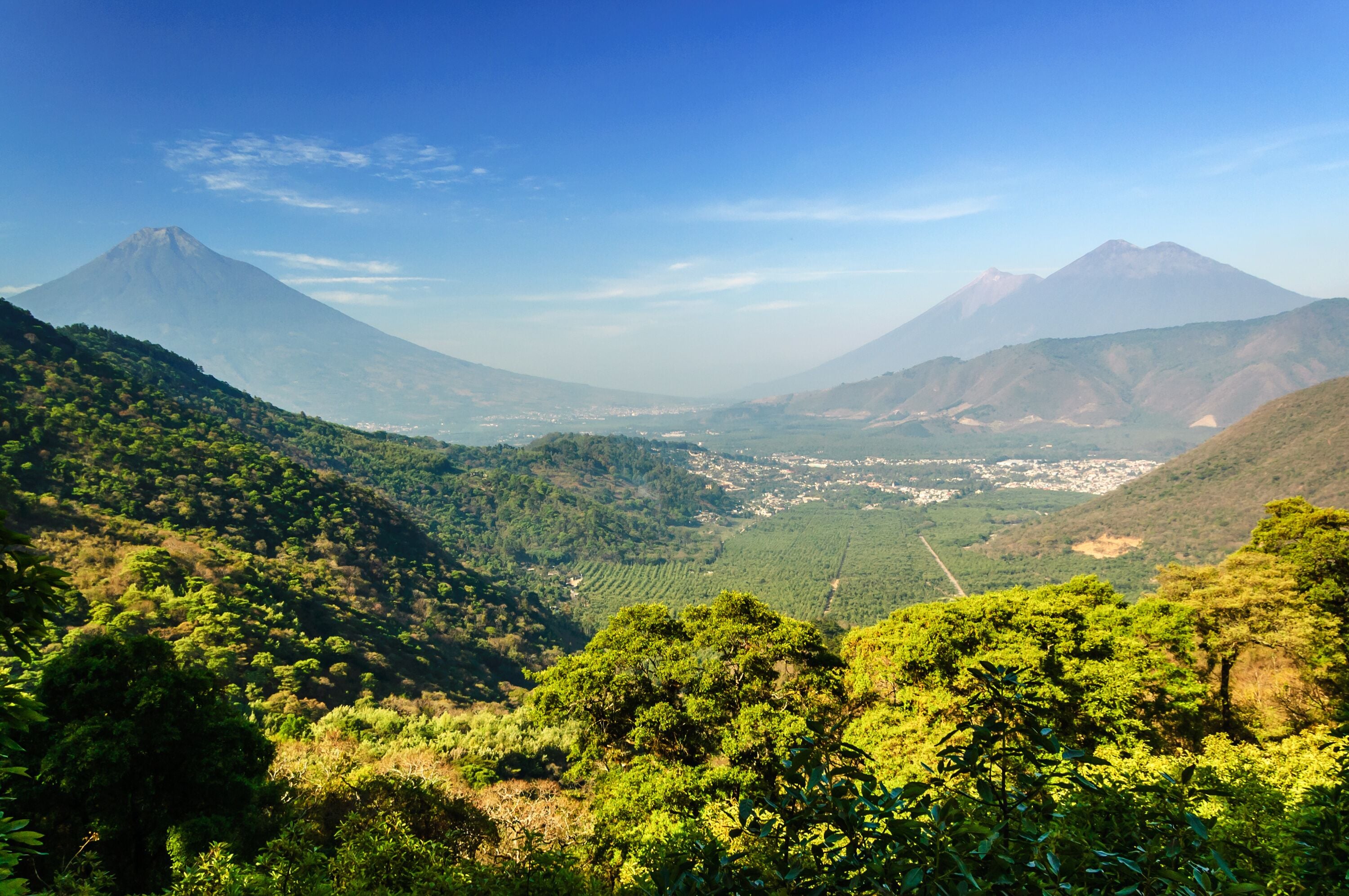 Paisagem montanhosa com florestas verdes densas e um vale com edifícios dispersos.