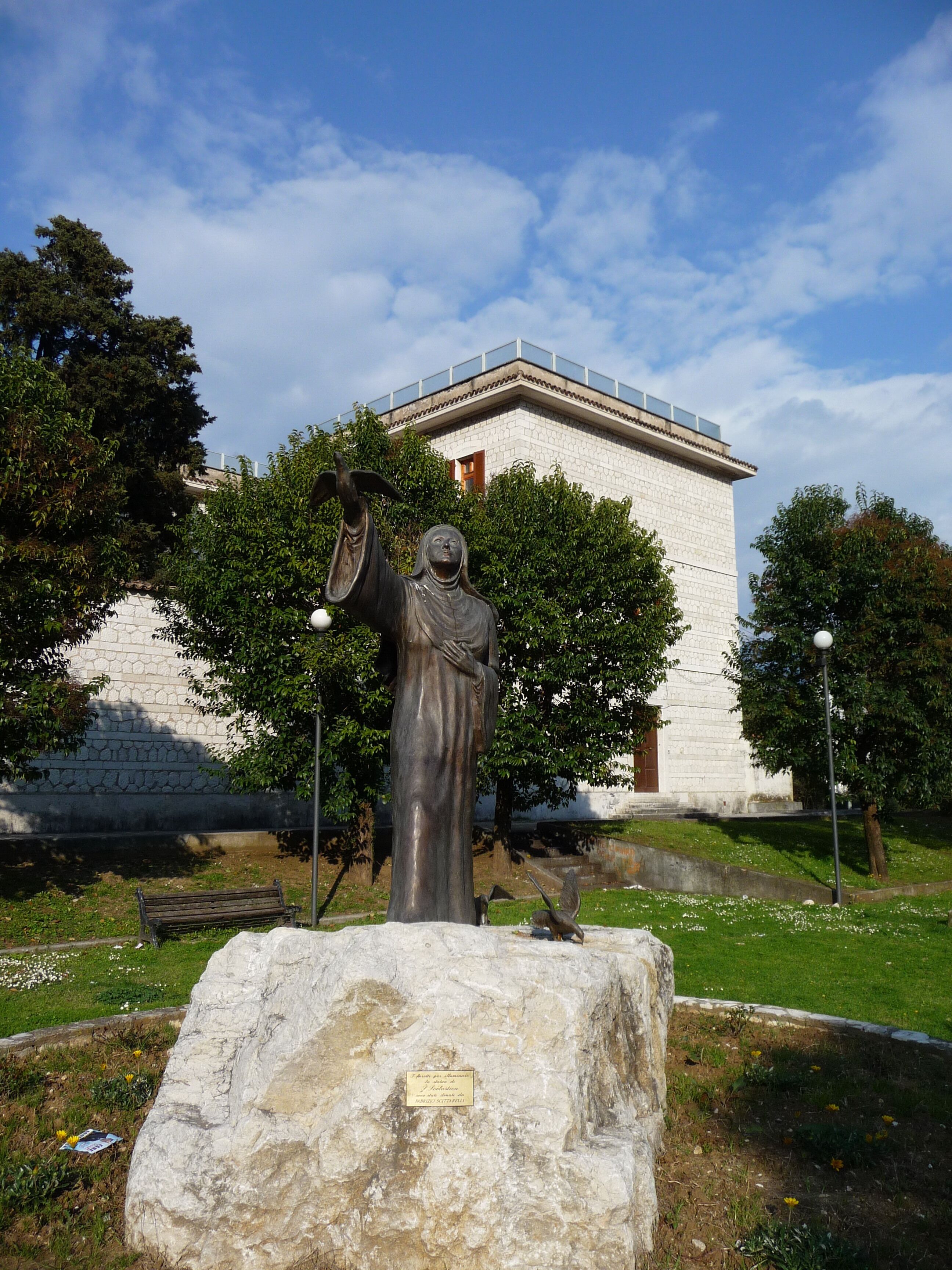 Uma estátua de mulher segurando uma esfera, uma placa de pedra e um edifício ao fundo.