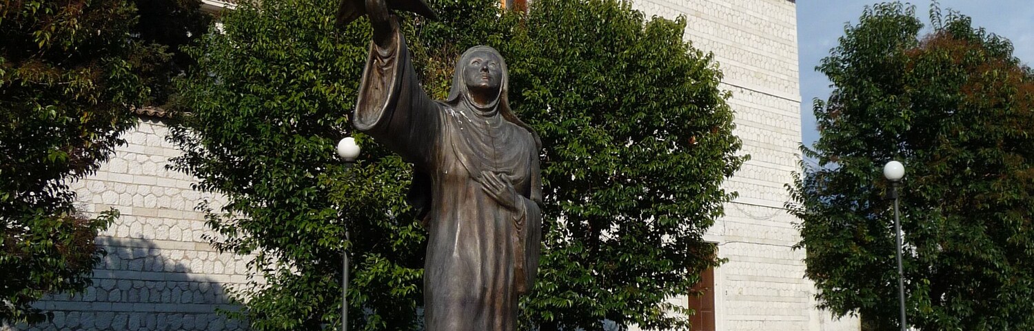 Uma estátua de mulher segurando uma esfera, uma placa de pedra e um edifício ao fundo.