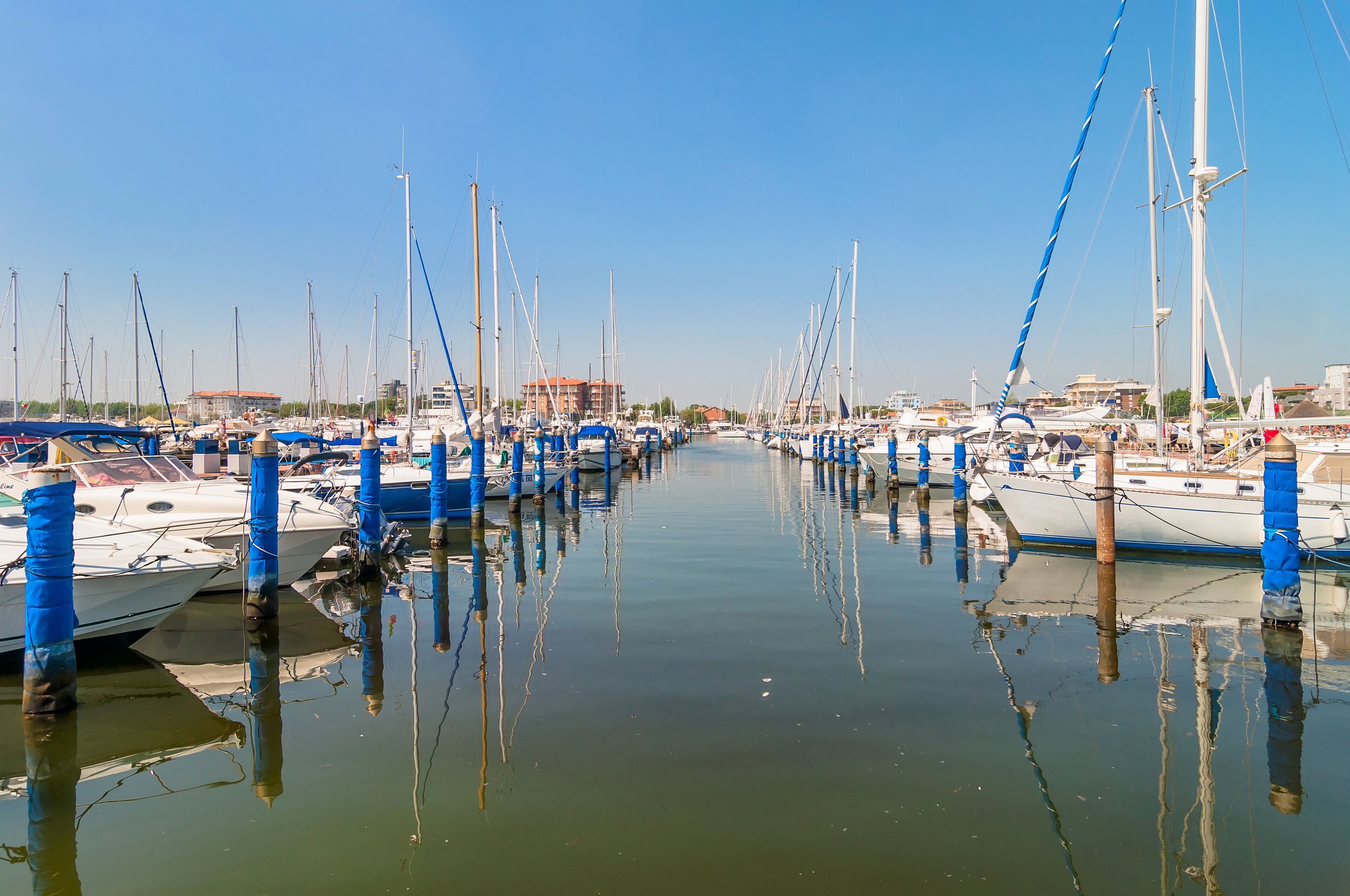 Uma marina com vários barcos atracados, água calma e céu azul claro.
