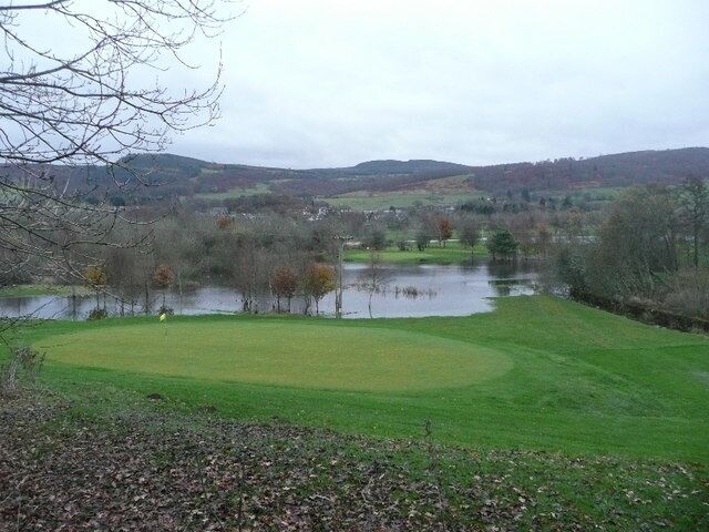 Um campo de golfe com um lago e colinas ao fundo.