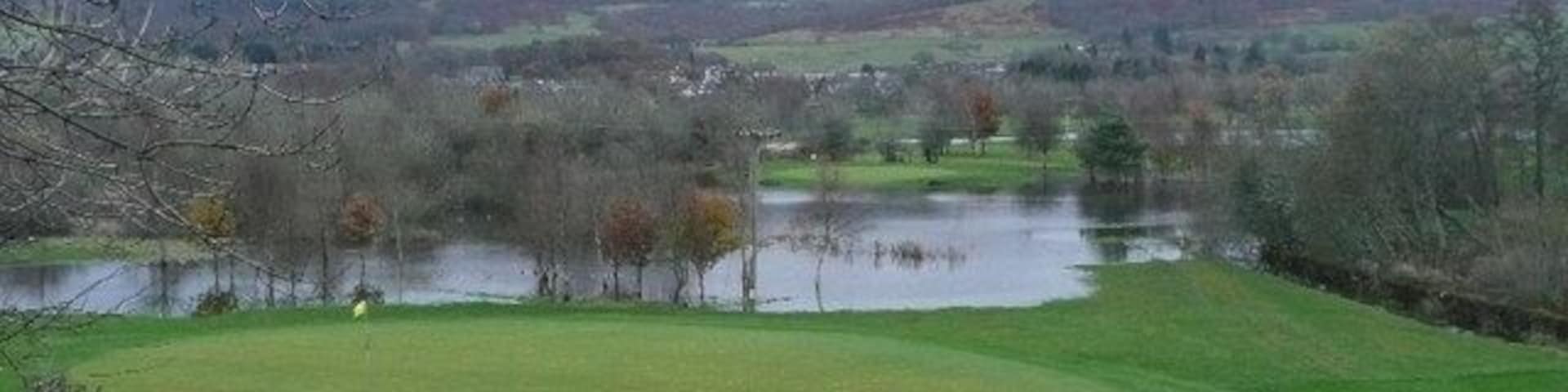 Um campo de golfe com um lago e colinas ao fundo.