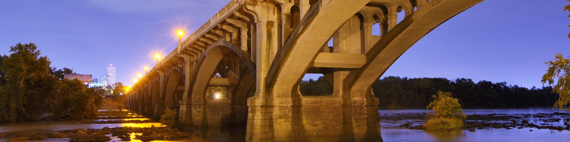 Uma ponte com várias arcos sobre um rio ao entardecer.