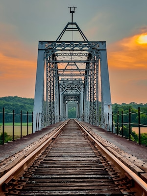Uma ponte ferroviária com estrutura metálica treliçada e linhas descendo ao longe.