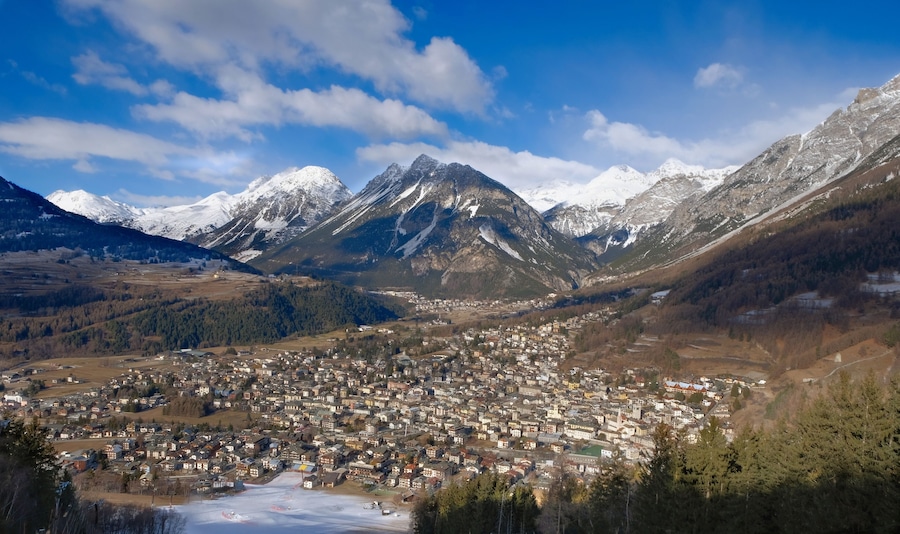 Uma cidade aninhada num vale, com montanhas cobertas de neve ao fundo.