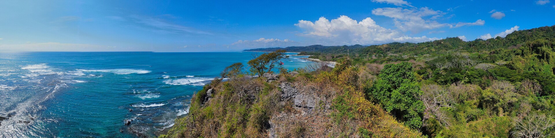 Paisagem costeira com céu azul límpido, mar turquesa e colinas verdes.
