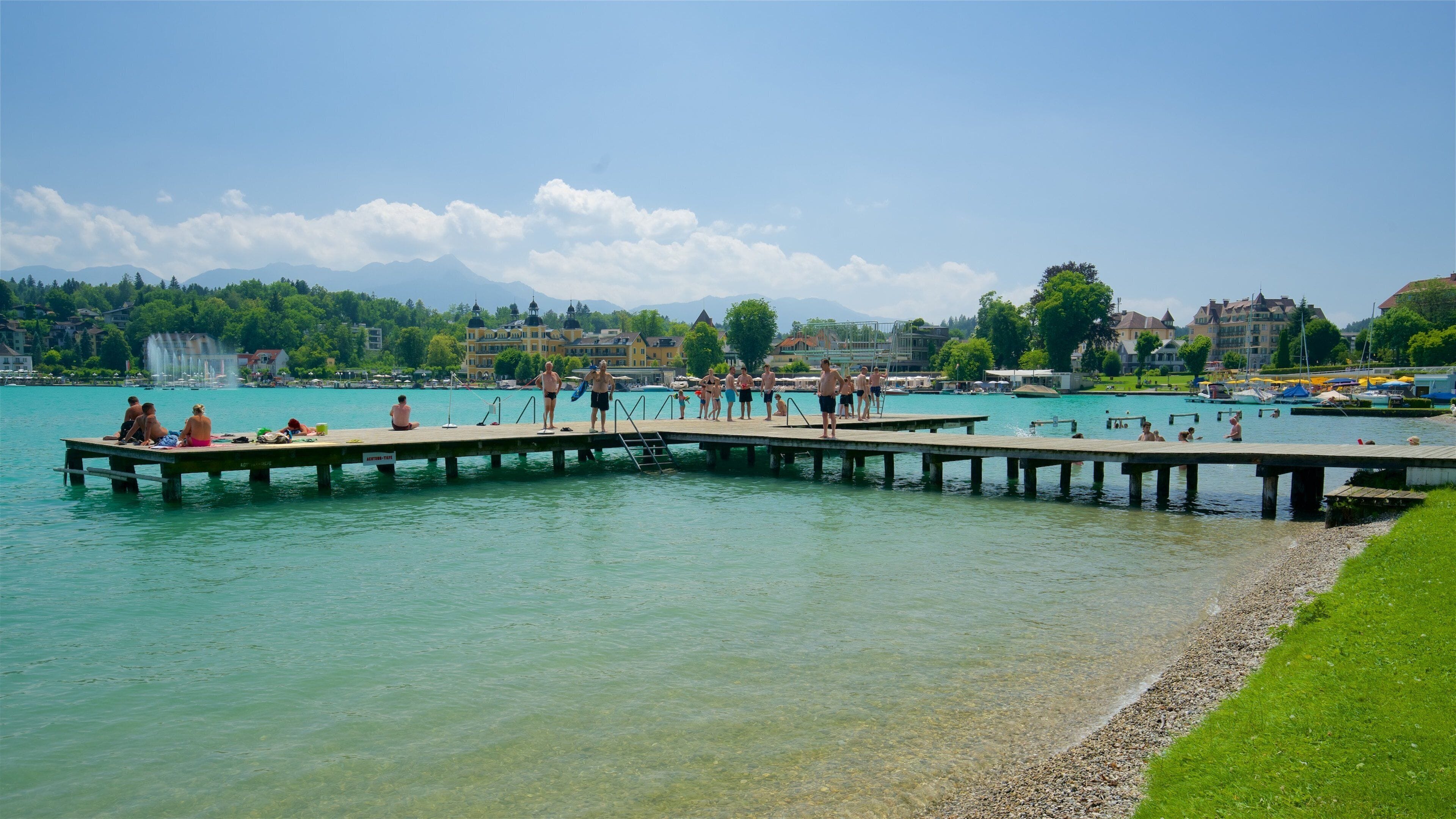 Um cais se estendendo sobre um lago azul-turquesa, com pessoas relaxando e nadando.