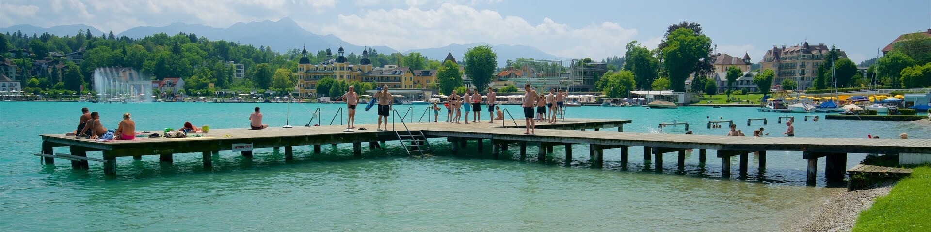 Um cais se estendendo sobre um lago azul-turquesa, com pessoas relaxando e nadando.
