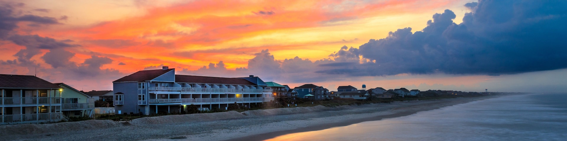 Uma praia com uma fileira de casas e um pôr do sol.