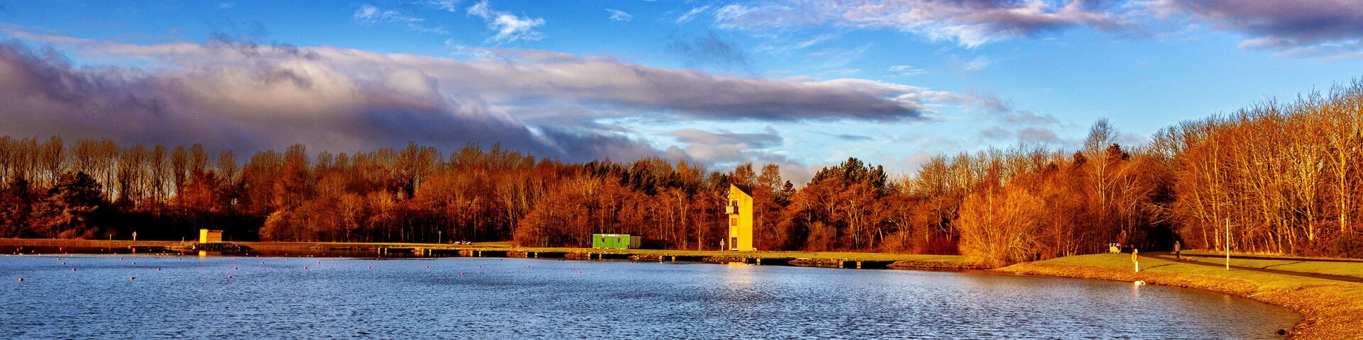 Um lago com um edifício amarelo e árvores ao fundo.