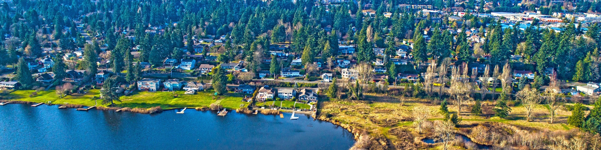Uma área residencial à beira de um lago, com casas, florestas densas e montanhas ao fundo.