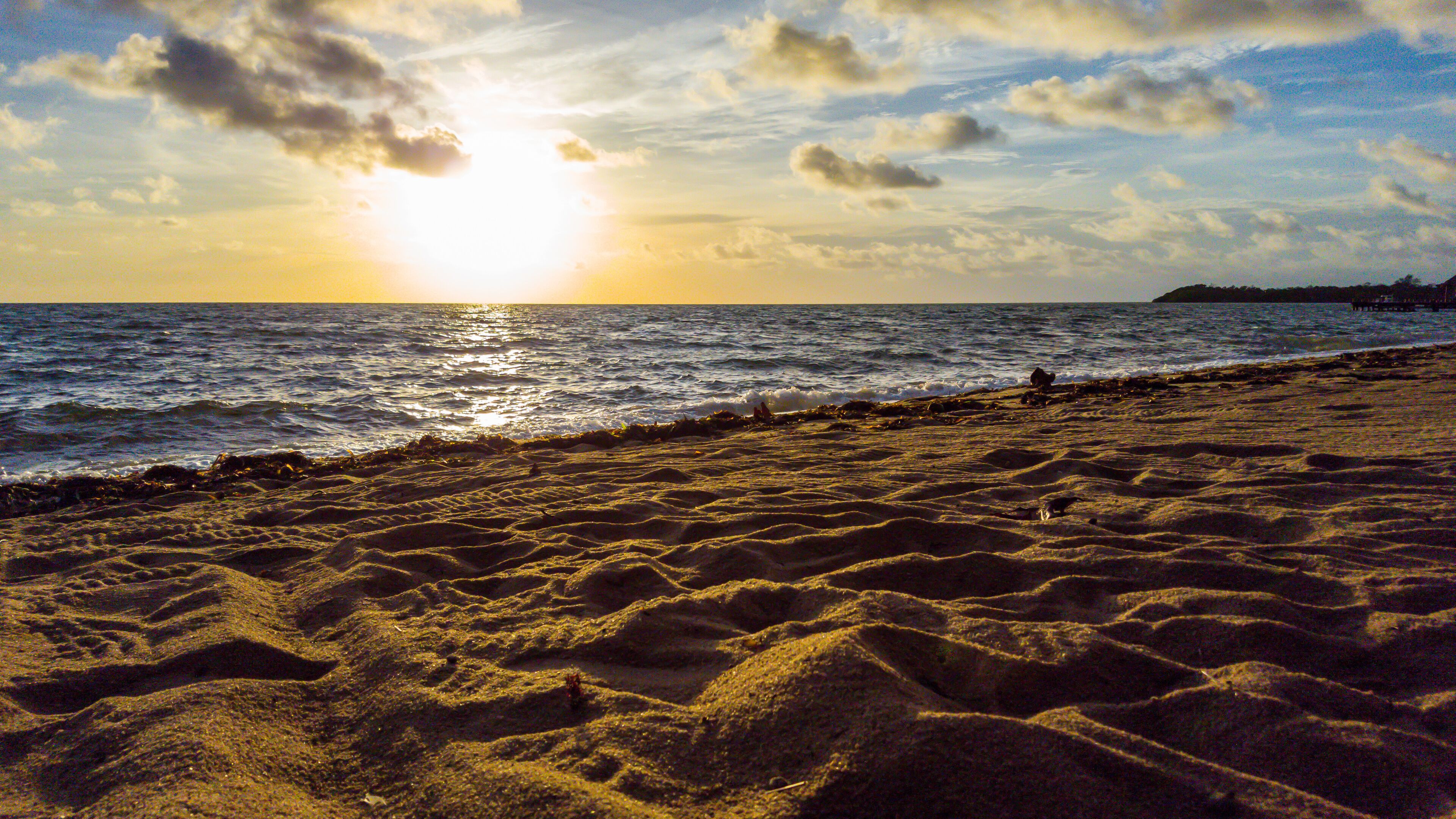 Praia com areia e ondas ao pôr do sol.