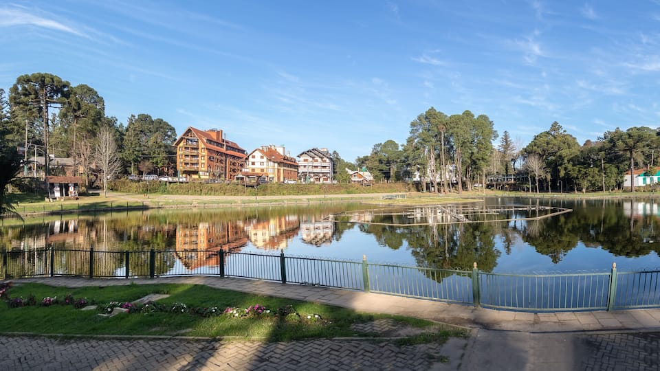 Um lago calmo com uma cerca, rodeado por edifícios e árvores.