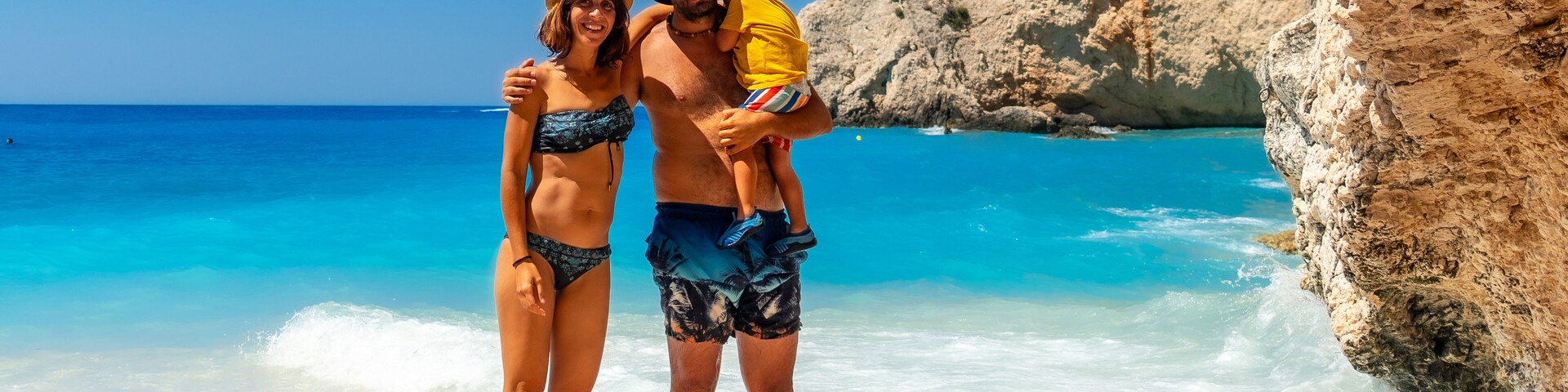 Uma praia com águas turquesa cristalinas, um penhasco rochoso e uma faixa costeira de pedras.