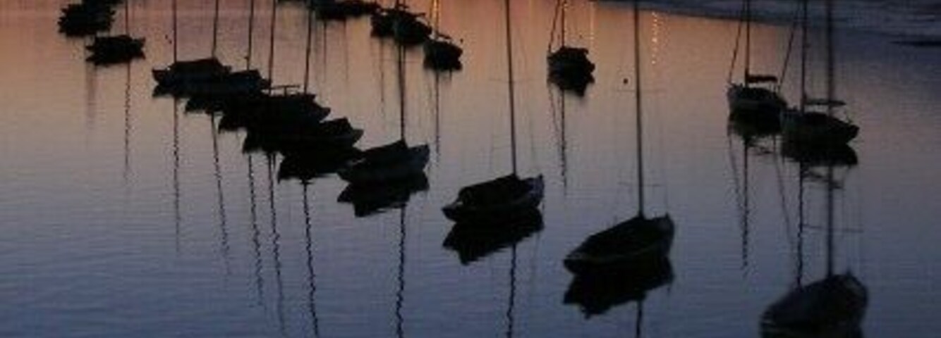 Um porto tranquilo ao entardecer, com vários barcos ancorados na água.