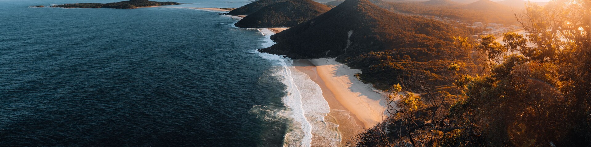 Paisagem costeira com praia, oceano e colinas arborizadas.