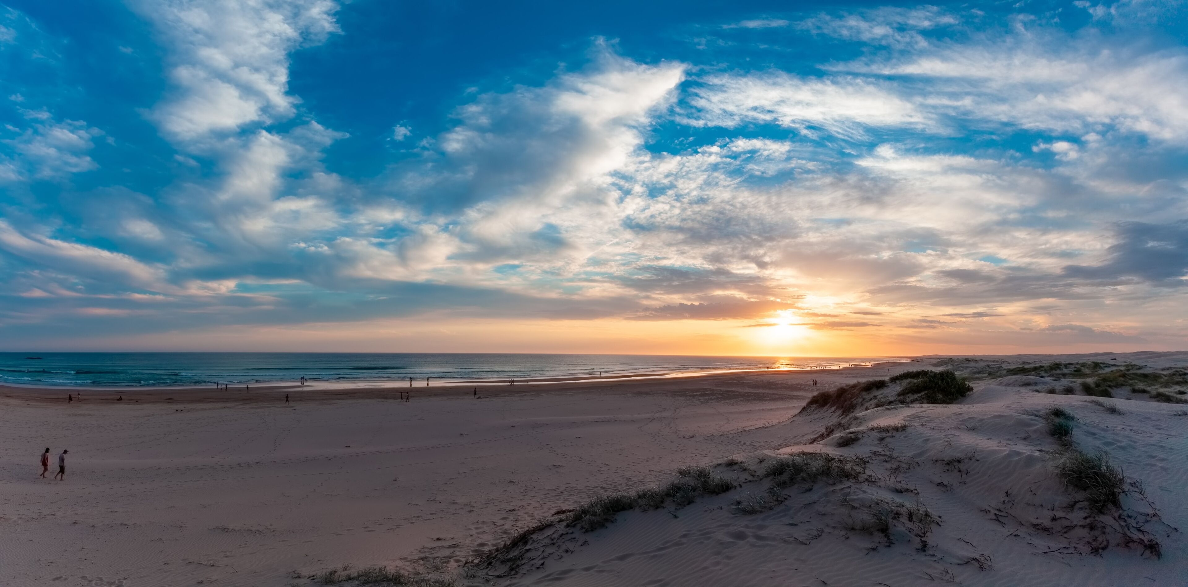 Uma praia com dunas de areia e um pôr do sol sobre o oceano.