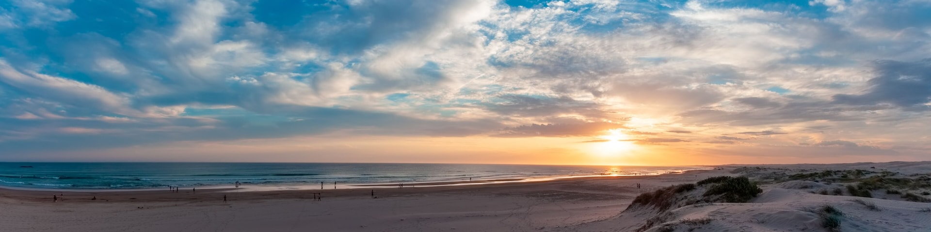Uma praia com dunas de areia e um pôr do sol sobre o oceano.