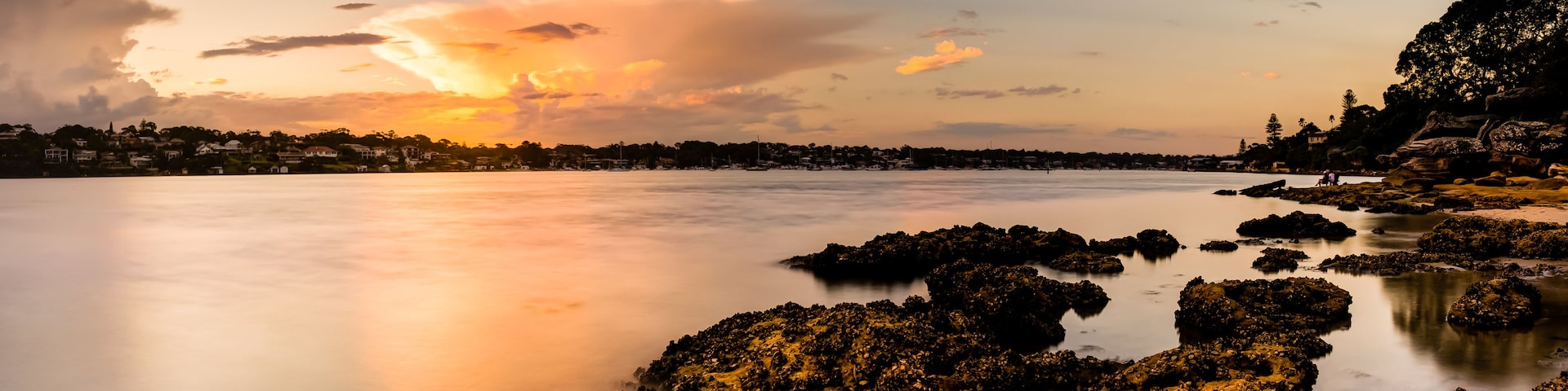 Paisagem costeira com mar calmo, afloramentos rochosos e um pôr do sol.