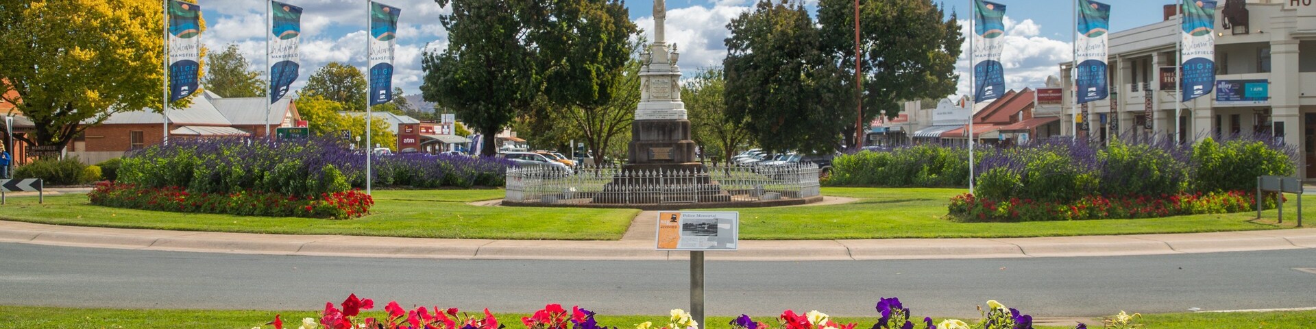 Um parque com um monumento, canteiros de flores coloridos e um céu azul límpido.