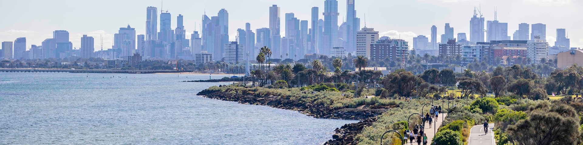 Paisagem costeira urbana com um horizonte imponente, um calçadão à beira-mar e um litoral rochoso.