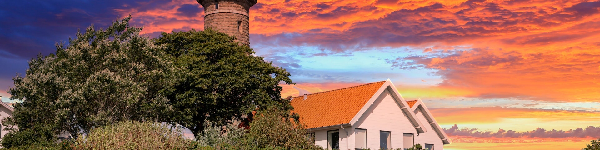 Um farol, um edifício branco e vegetação densa.