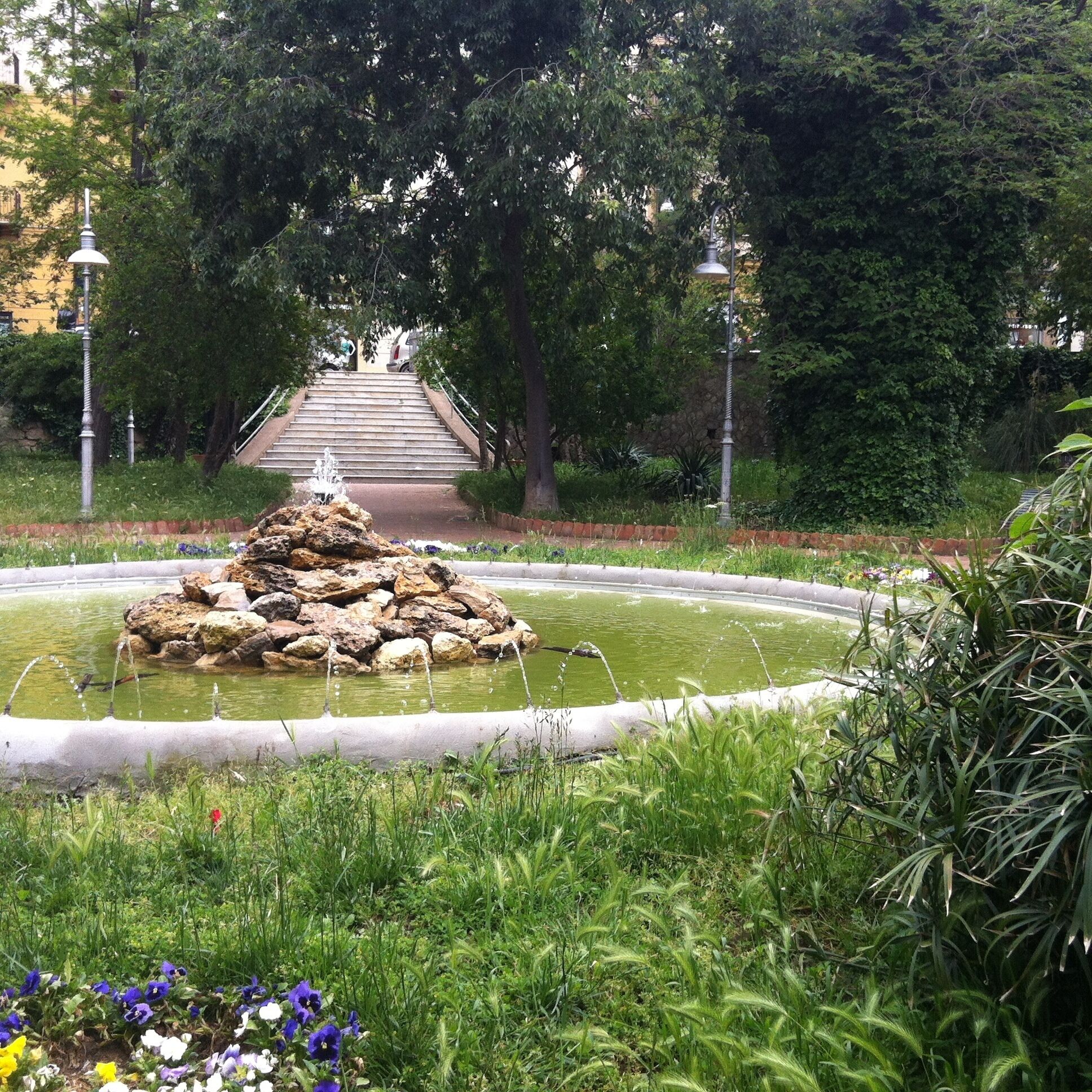 Um jardim com uma fonte, cercado por árvores e uma escadaria.