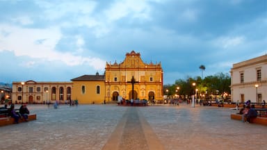 Uma praça histórica com uma igreja imponente, arquitetura ornamentada e uma cruz central.