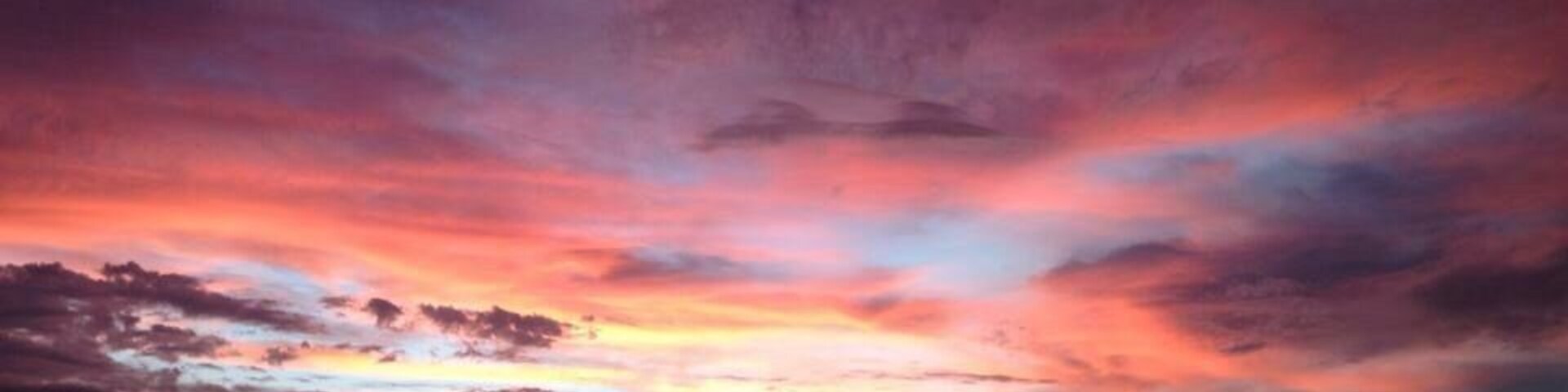 Um pôr do sol sobre um mar calmo, com veleiros e silhuetas de pessoas.