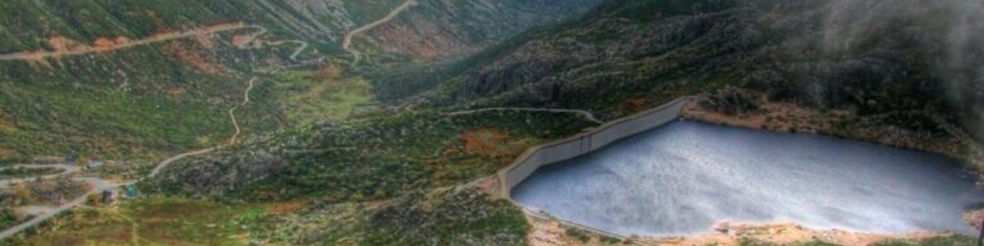 Paisagem montanhosa com um lago e uma estrada sinuosa.