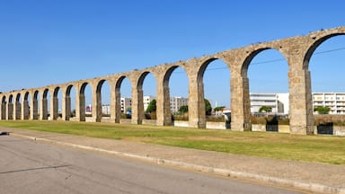 Uma série de arcos de pedra ao longo de uma estrada, com edifícios ao fundo.