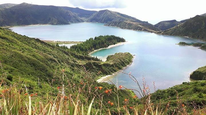 Um lago rodeado por colinas verdes e uma praia.