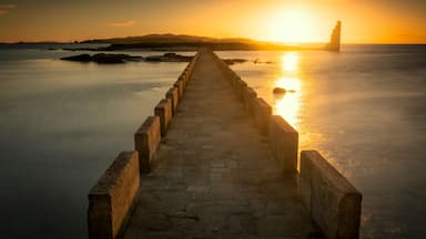 Um cais de pedra que leva a um farol à beira-mar ao pôr do sol.