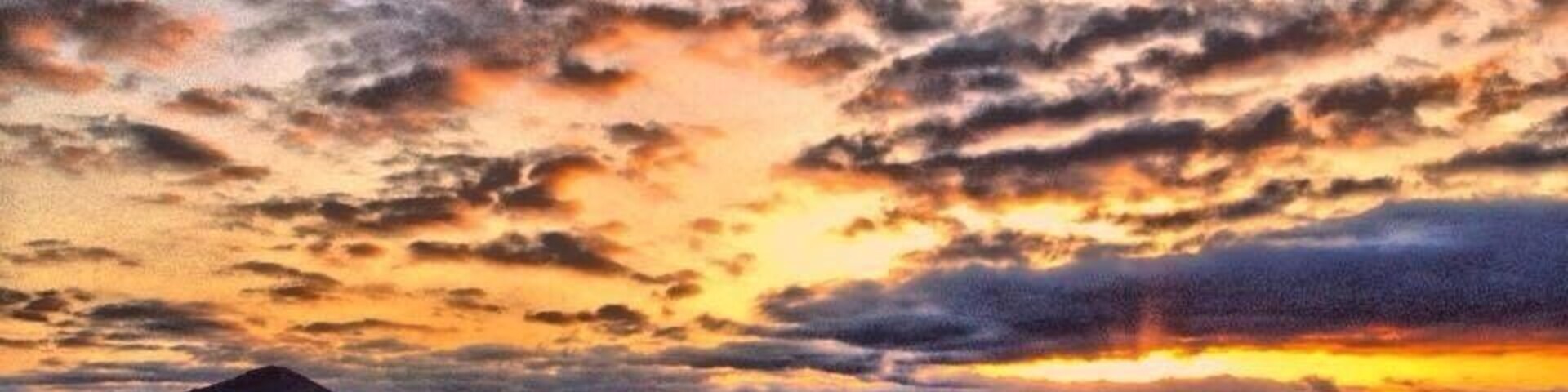 Pôr do sol sobre a água, com uma montanha ao fundo e edifícios na orla.