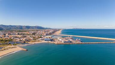 Paisagem costeira com praia, porto e montanhas ao fundo.
