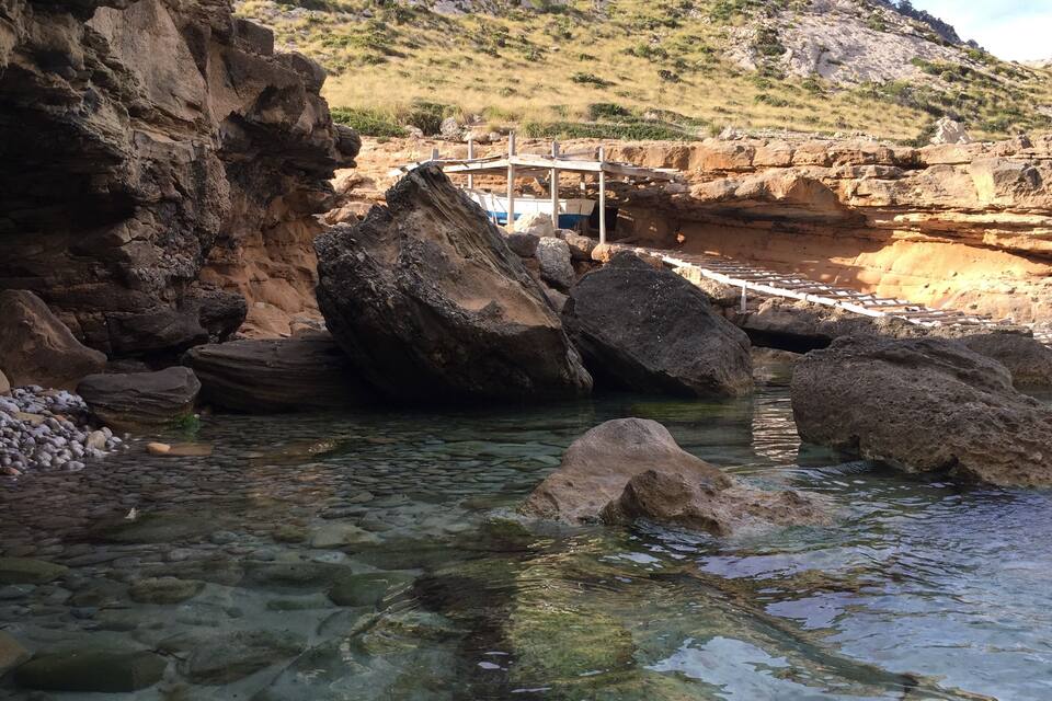 Uma costa rochosa com águas claras, grandes pedras e uma estrutura de madeira.