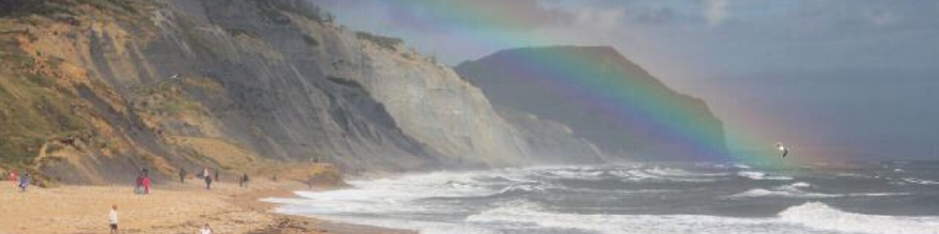 Rainbow at Charmouth Beach The rainbow appears to pass in front of the distant Golden Cap, the highest point on England's south coast. The rainbow is due to spray being whipped off the sea by high onshore winds.