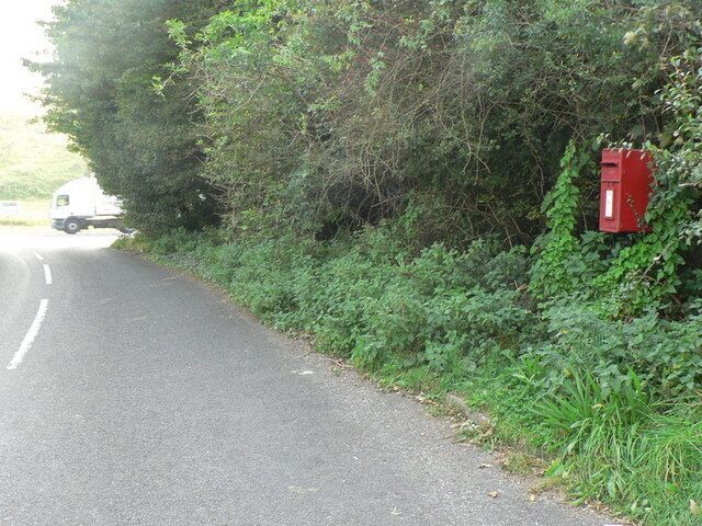 Uma estrada rural com um caminhão branco, vegetação densa e uma caixa de correio vermelha.