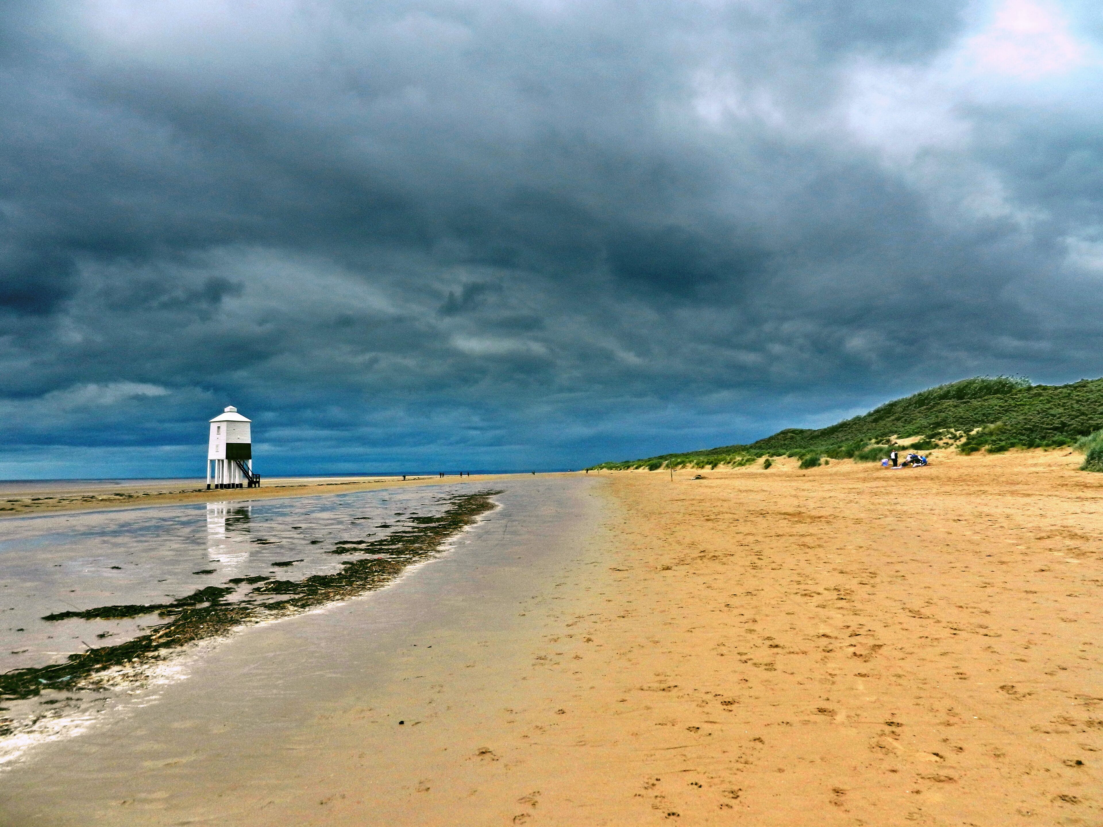Uma praia com um farol, areal arenoso e céu nublado.