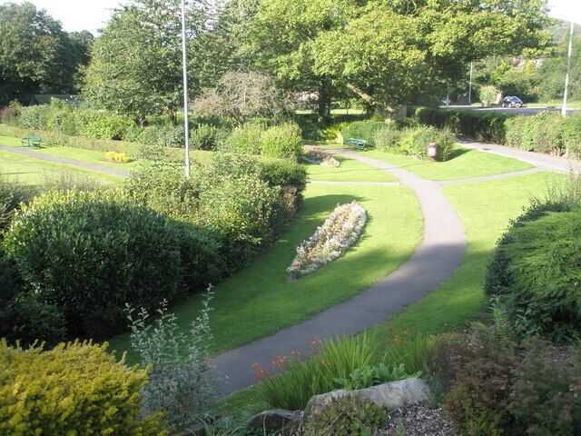 Um jardim paisagístico com um caminho sinuoso, gramados verdes e diversos arbustos.