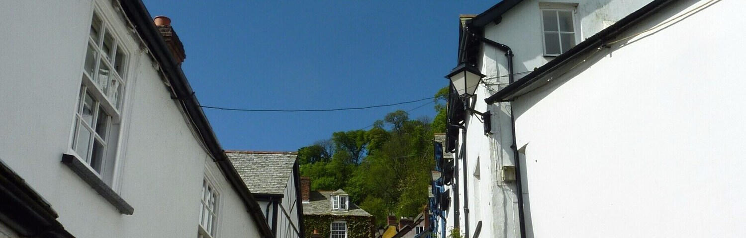 Uma rua de paralelepípedos estreita, ladeada por edifícios brancos com molduras de janela e chaminés pretas.